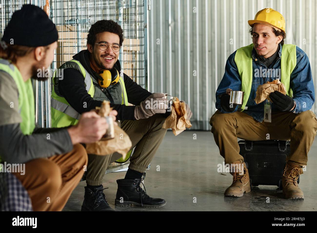 Happy young engineer with sandwich and cup of hot tea chatting to ...