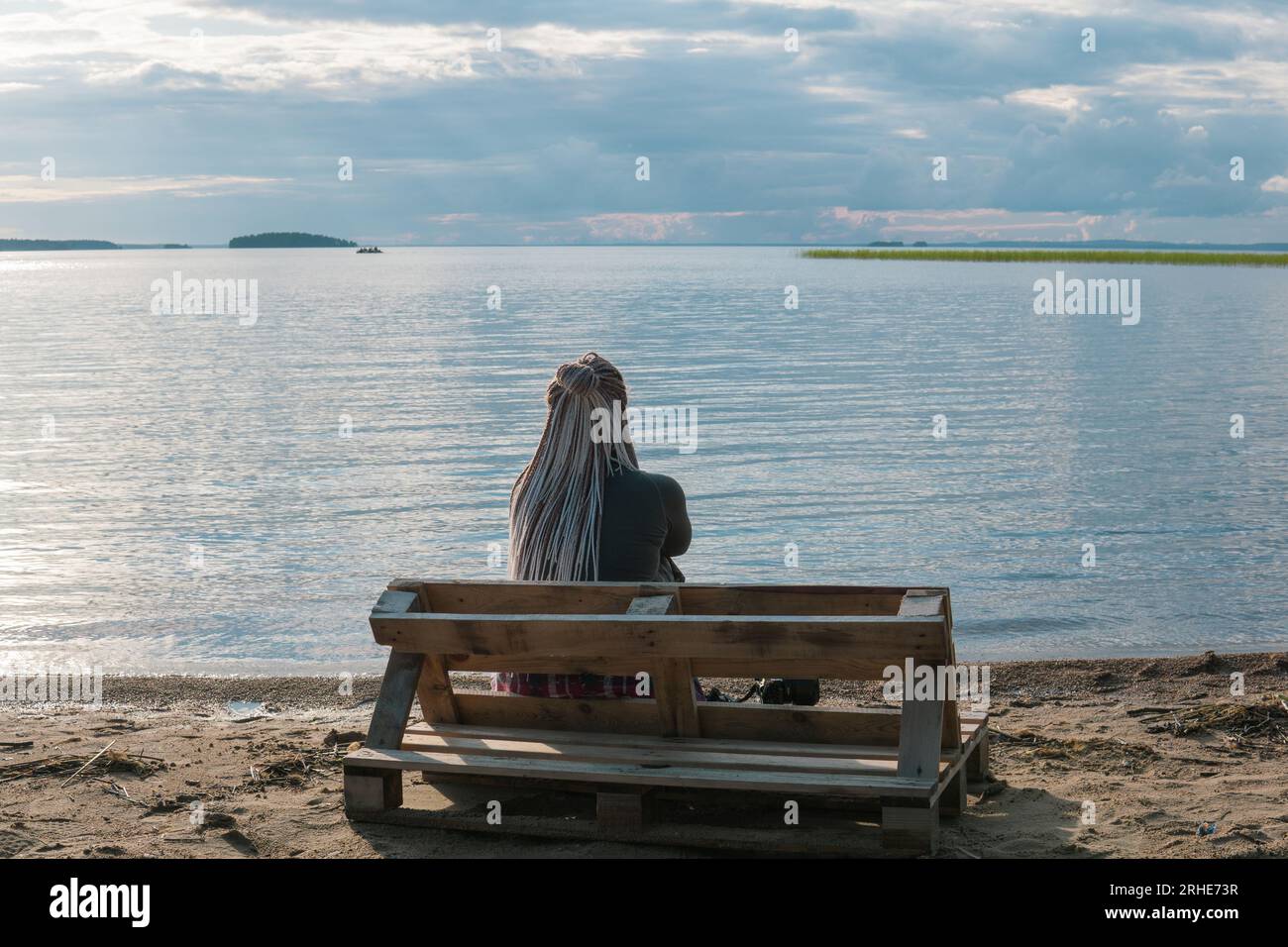 Sandy Beach On The Shore Of A Vast Lake A Woman Traveler Is Sitting On