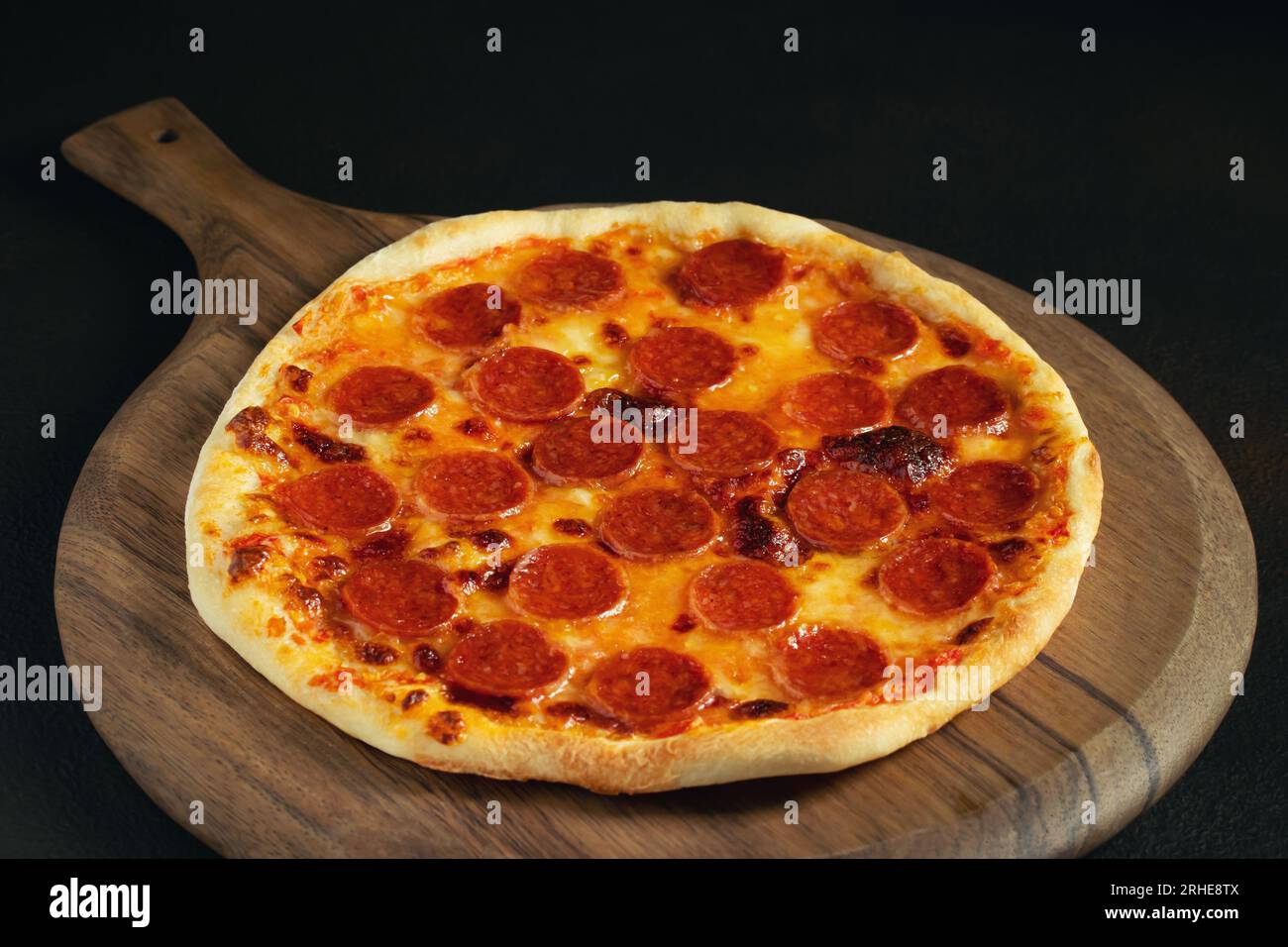 An uneven and slightly burnt homemade pepperoni pizza on a wooden tray ...