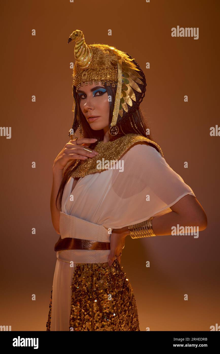 Elegant woman in egyptian look and headdress looking at camera on brown ...