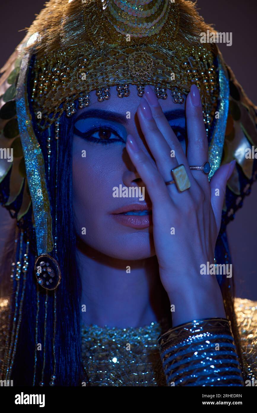 Portrait of woman in Egyptian headdress covering face and posing on ...