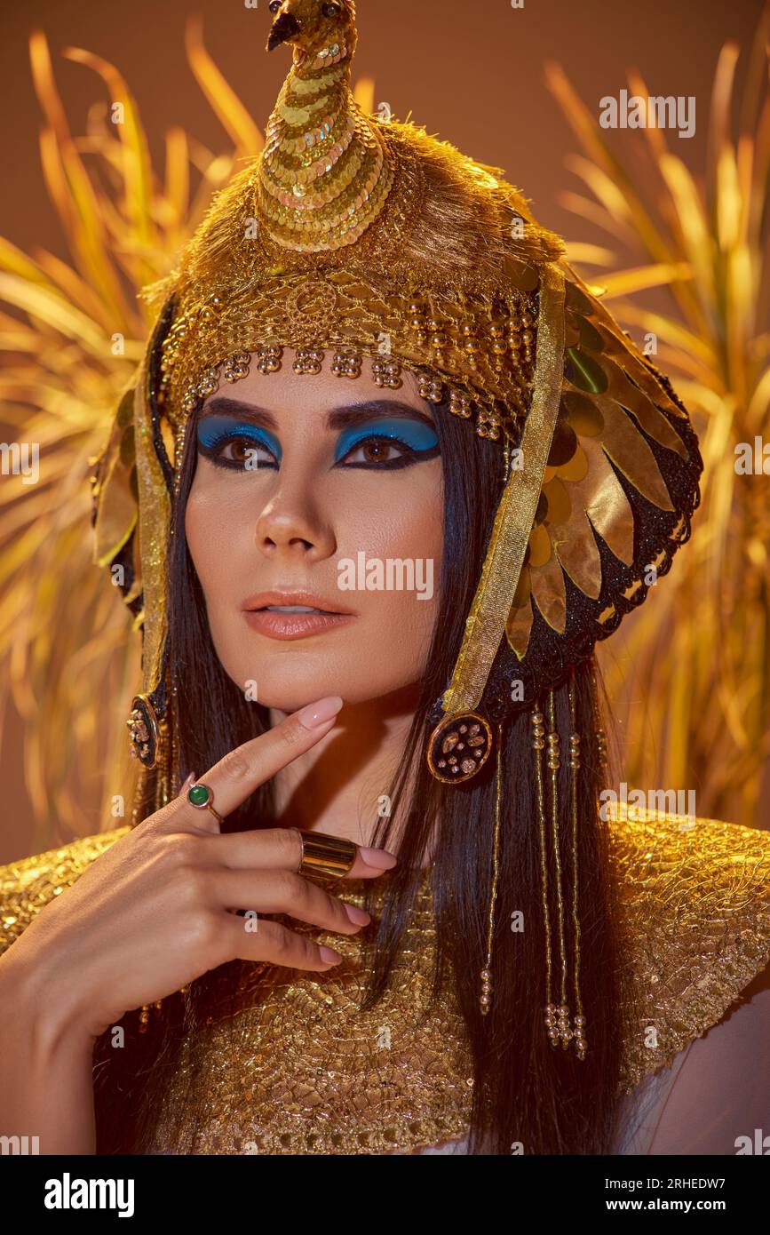 Elegant woman in egyptian look and headdress posing near blurred plants ...