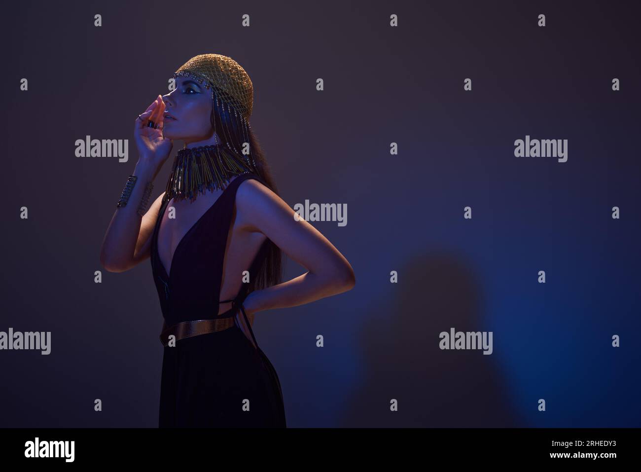 Elegant model in egyptian attire and headdress posing in blue light on ...