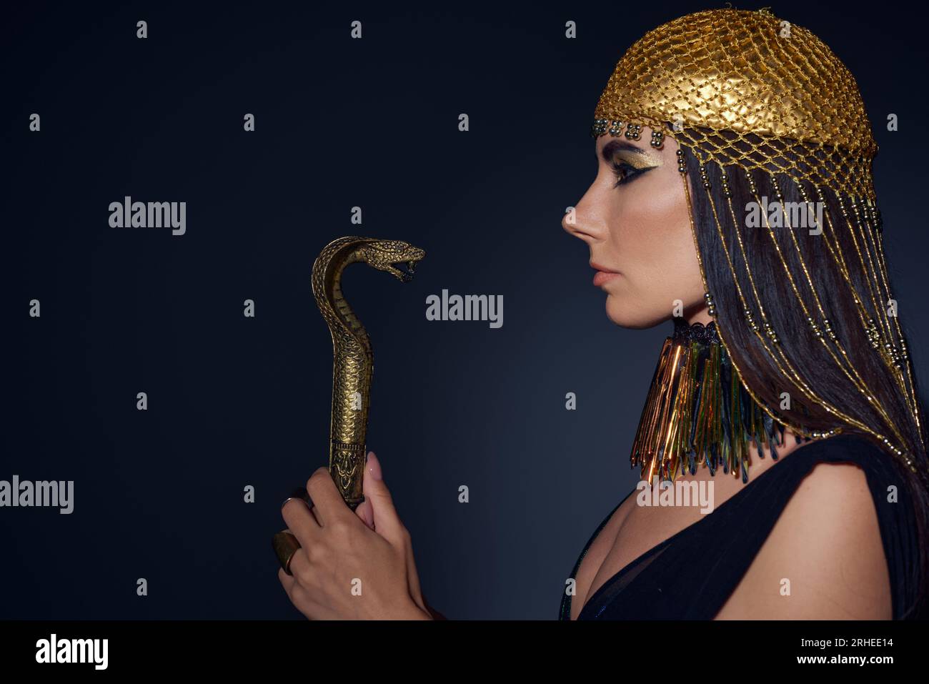 Side view of woman in egyptian attire holding crook in snake shape on blue background Stock ...