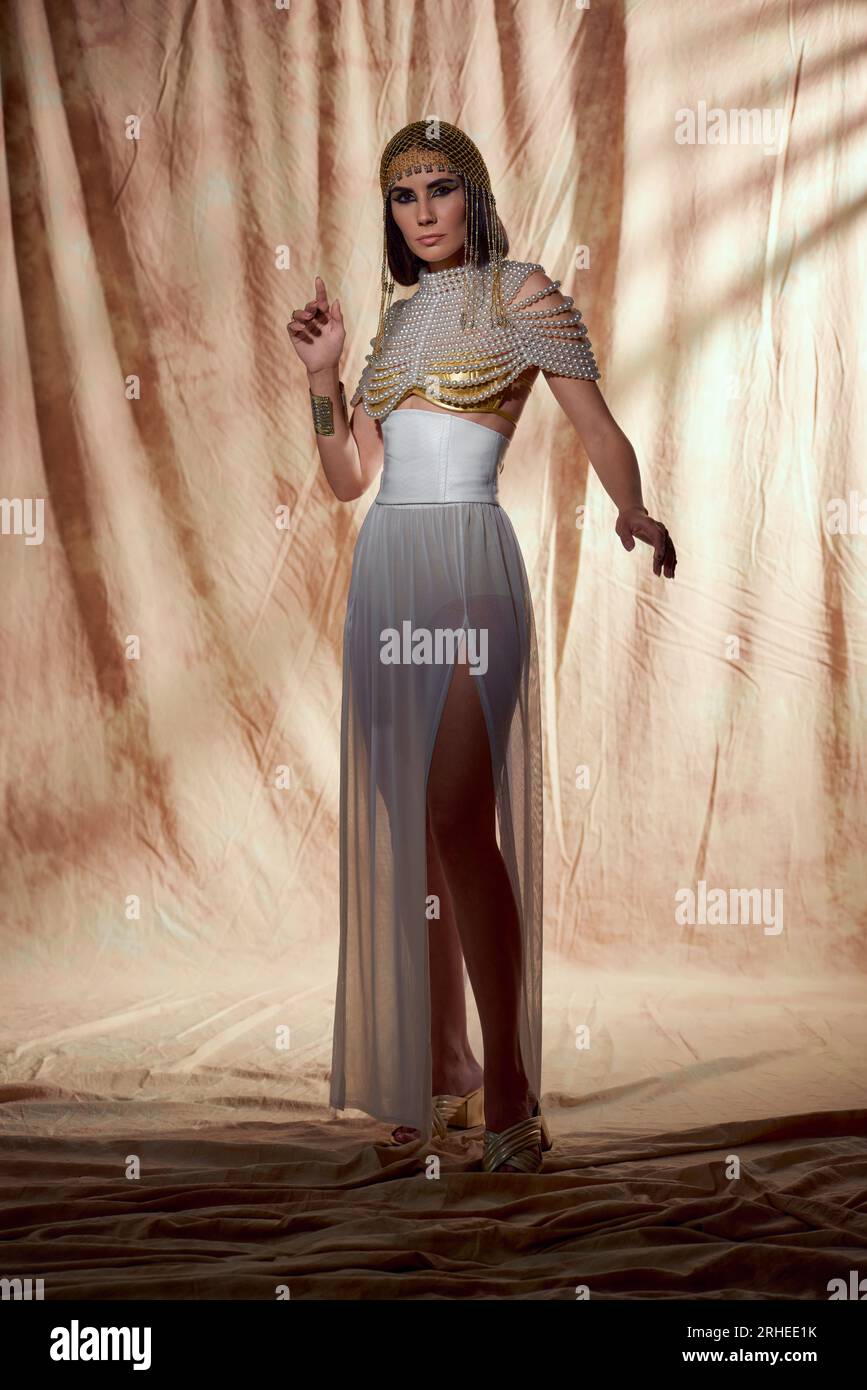 Trendy model in egyptian attire and pearl top posing while standing on ...