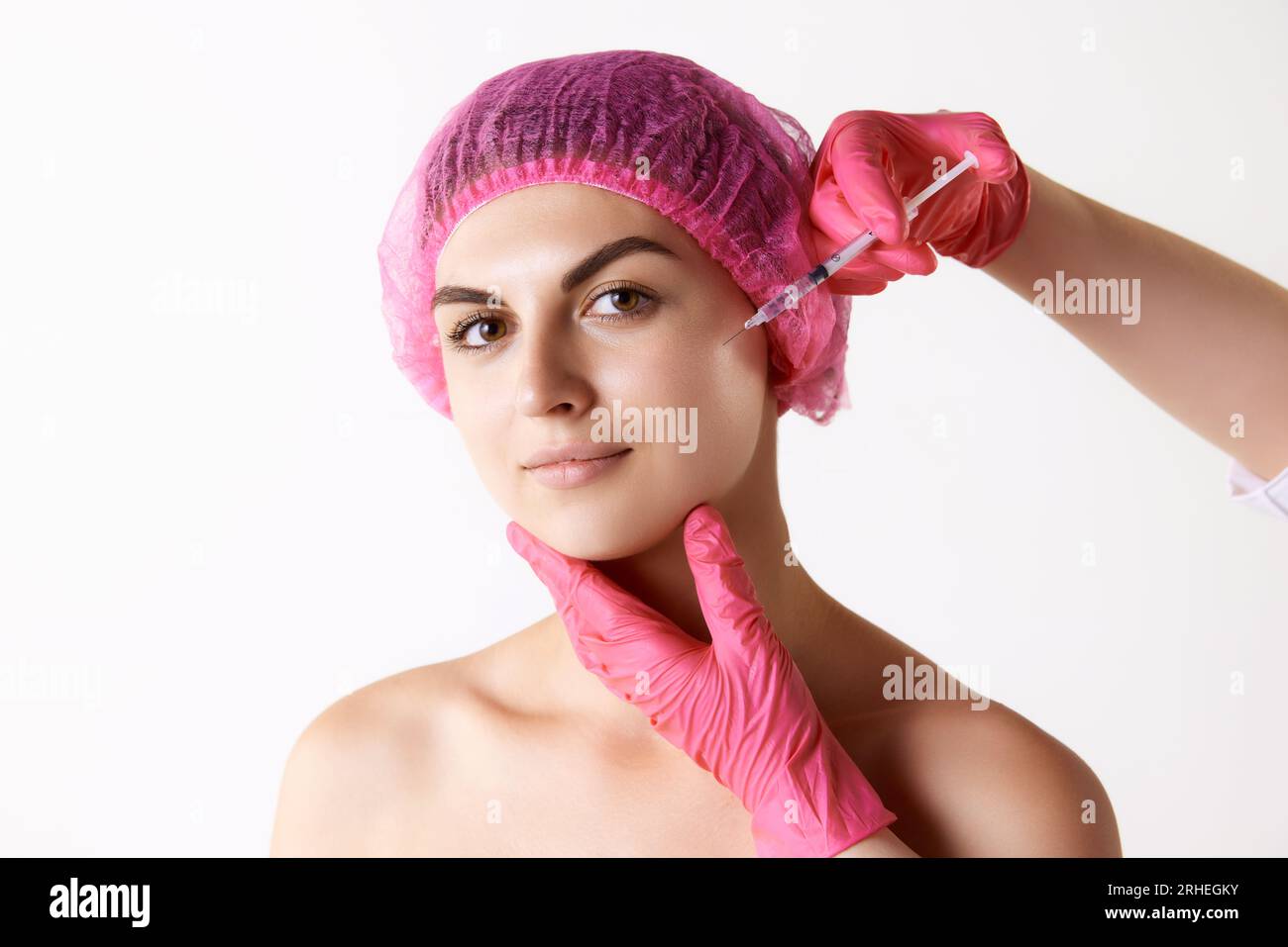 Young woman doing cosmetological injection on face against white studio ...