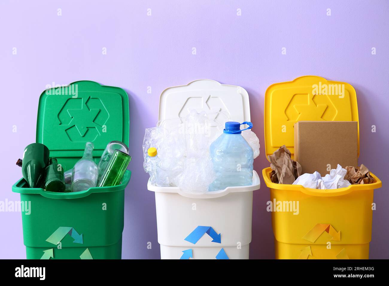 Containers with different types of garbage on lilac background ...