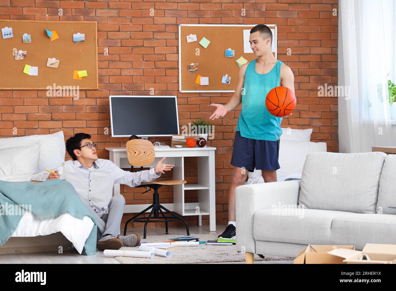 Sporty teenage boy with ball and his classmate studying in dorm room ...