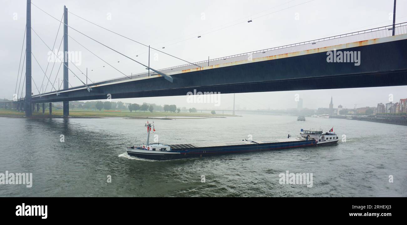 A bridge over the Rhine on a rainy day. A loaded barge sails under the ...