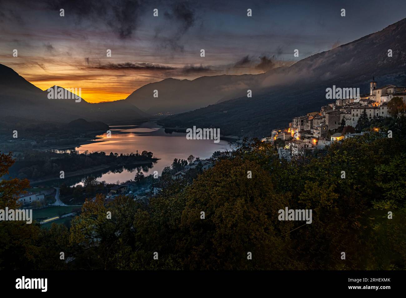 A fiery red sunset is reflected on Lake Barrea and illuminates the town ...