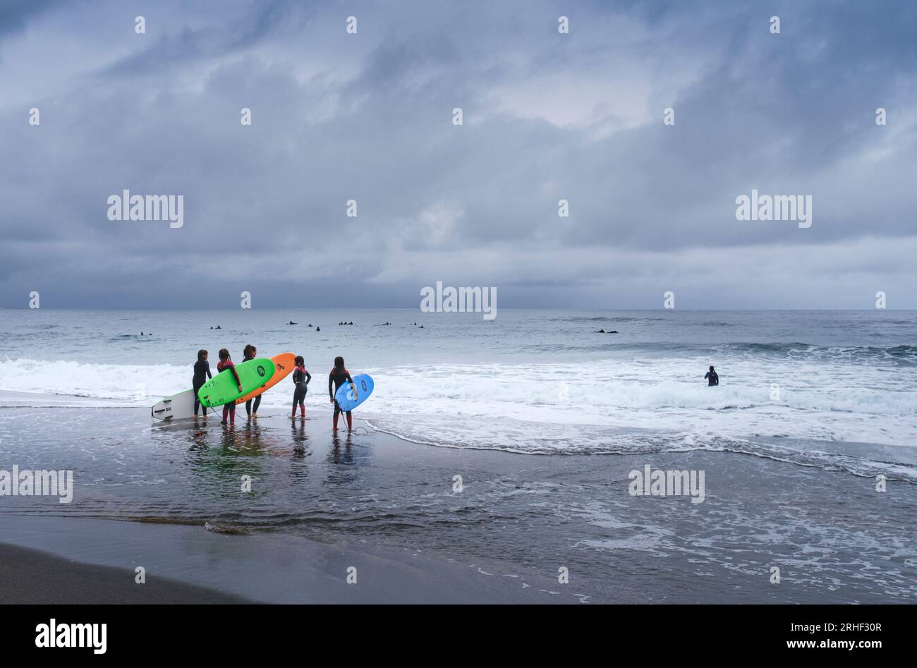 View of a beach in Asturias with young surfers with their brightly ...