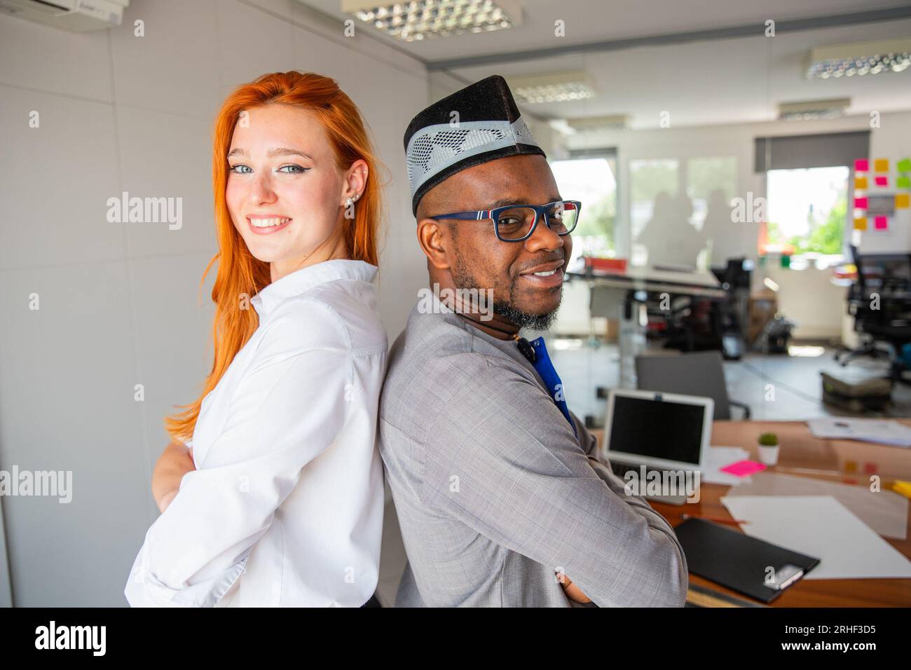 Two colleagues posing smiling in the office back to back, corporate ...