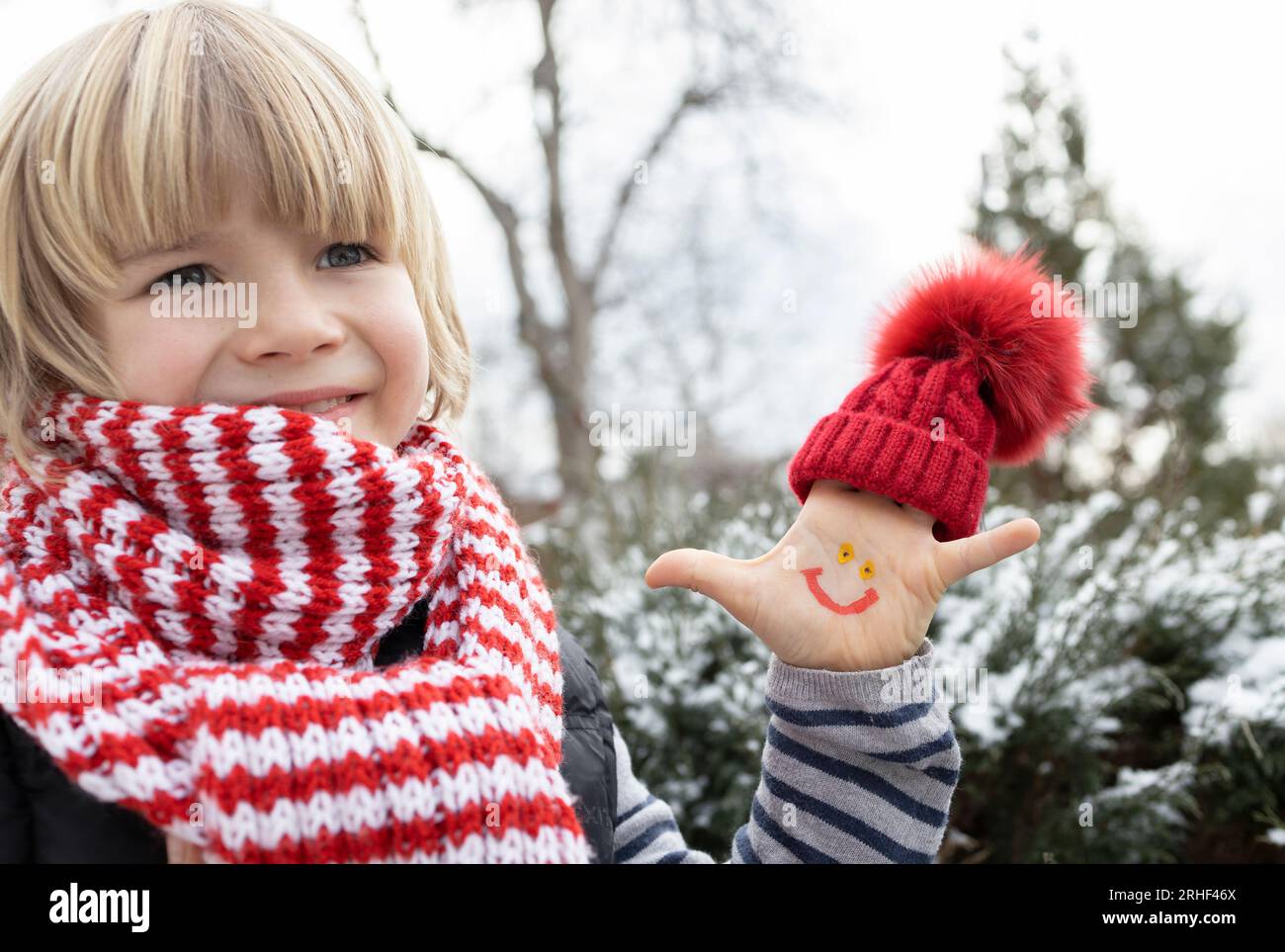 child wrapped in striped red scarf, smiling face is drawn on palm of ...