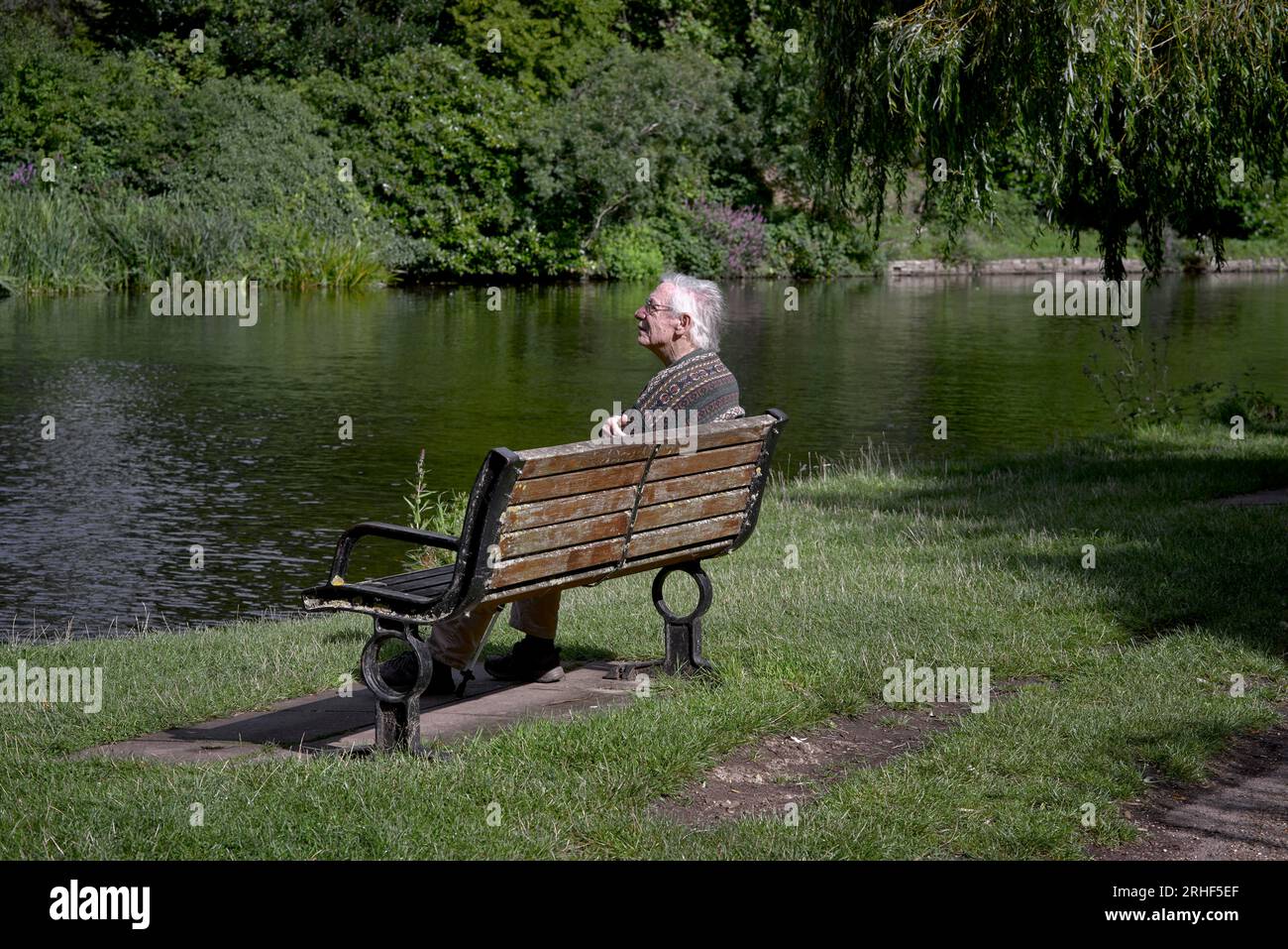 Senior man sitting on a park bench by the river, alone outside and ...