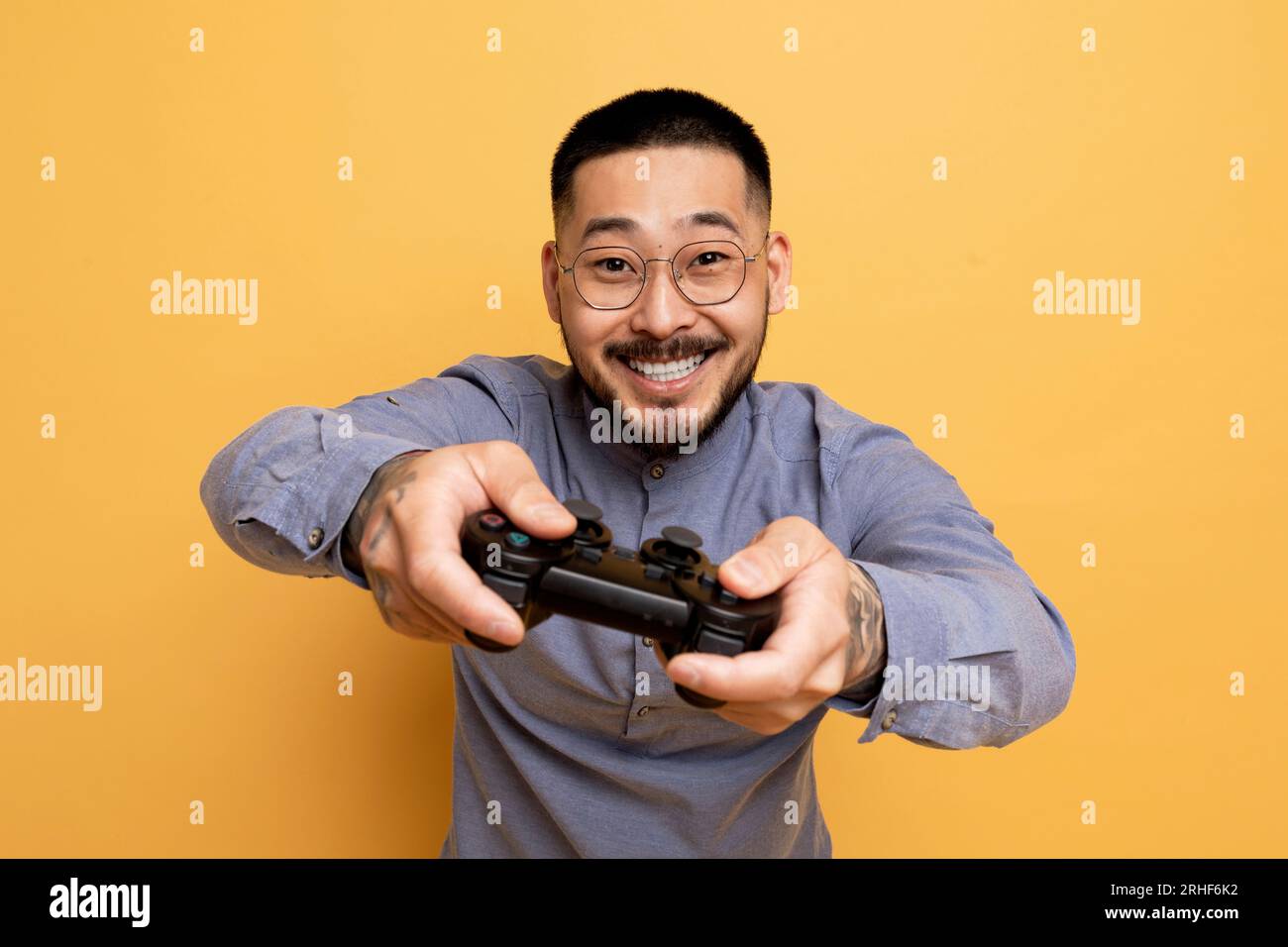 Excited asian guy playing video games with joystick over yellow studio ...