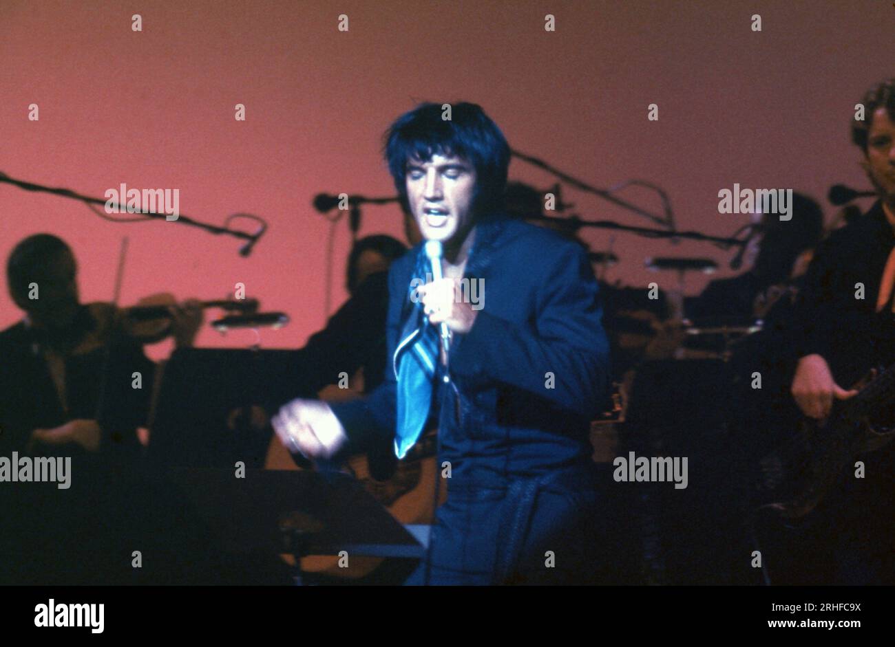 Elvis Presley wearing black with blue scarf, singing on stage, circa ...