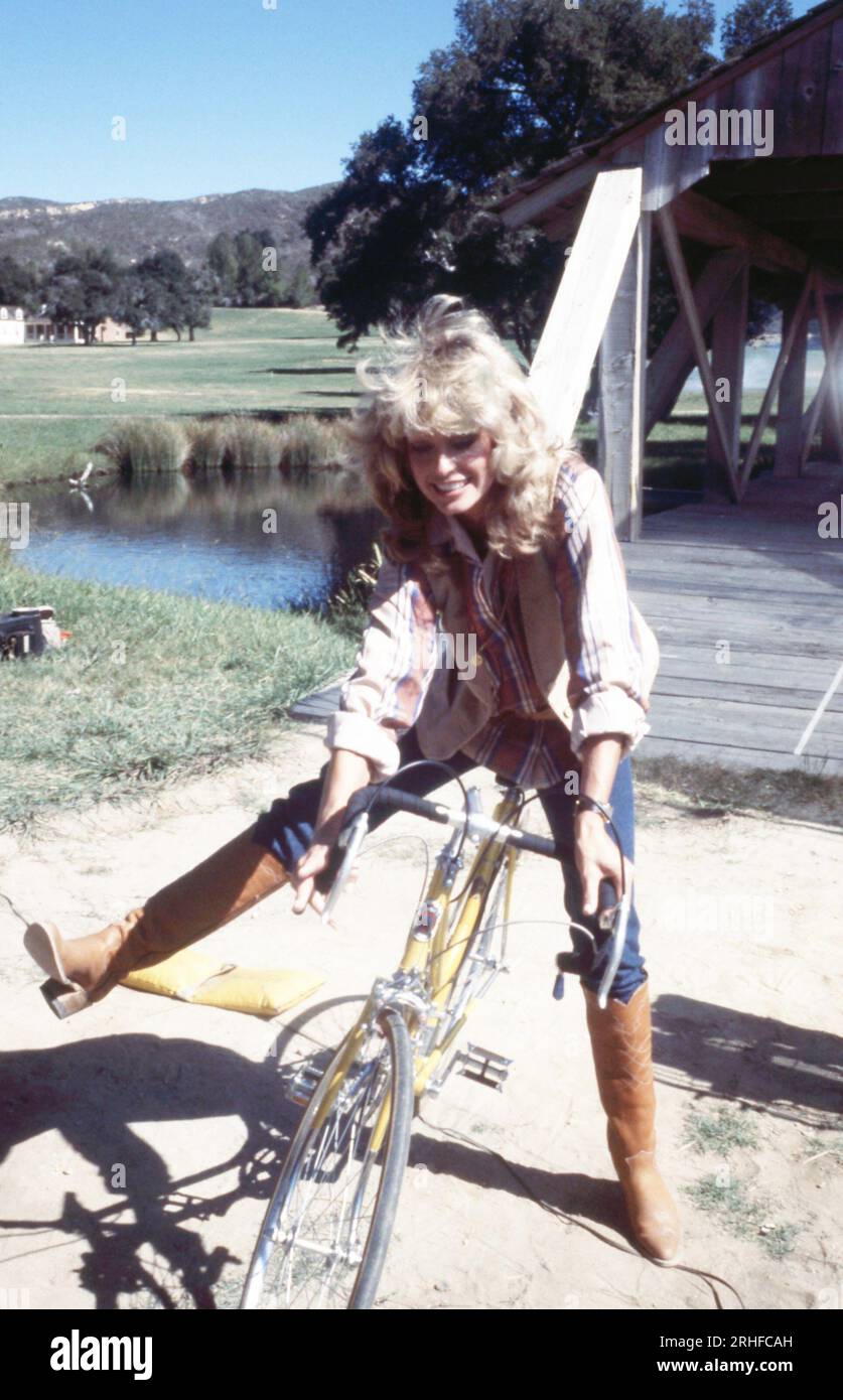 Farrah Fawcett smiling, wearing jeans, riding a bicycle, during the ...