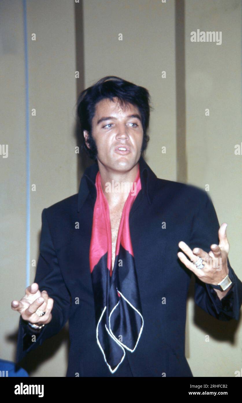 Elvis Presley in close-up, wearing a black jacket and scarf, gesturing ...