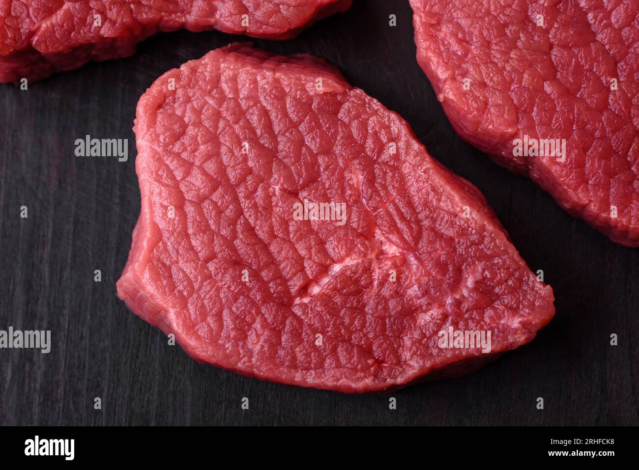Juicy fresh raw beef meat with salt, spices and herbs on a dark ...