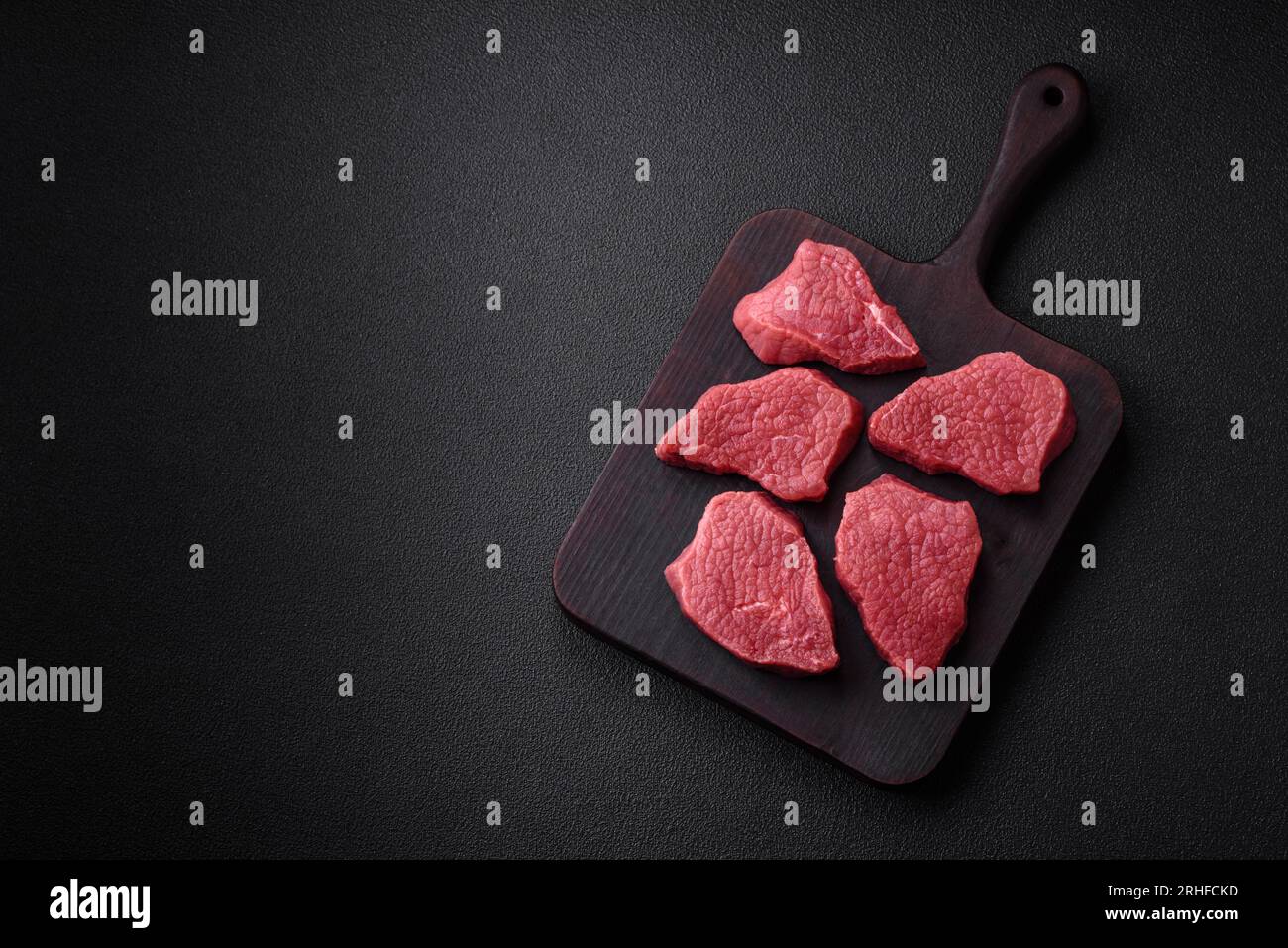 Juicy fresh raw beef meat with salt, spices and herbs on a dark ...
