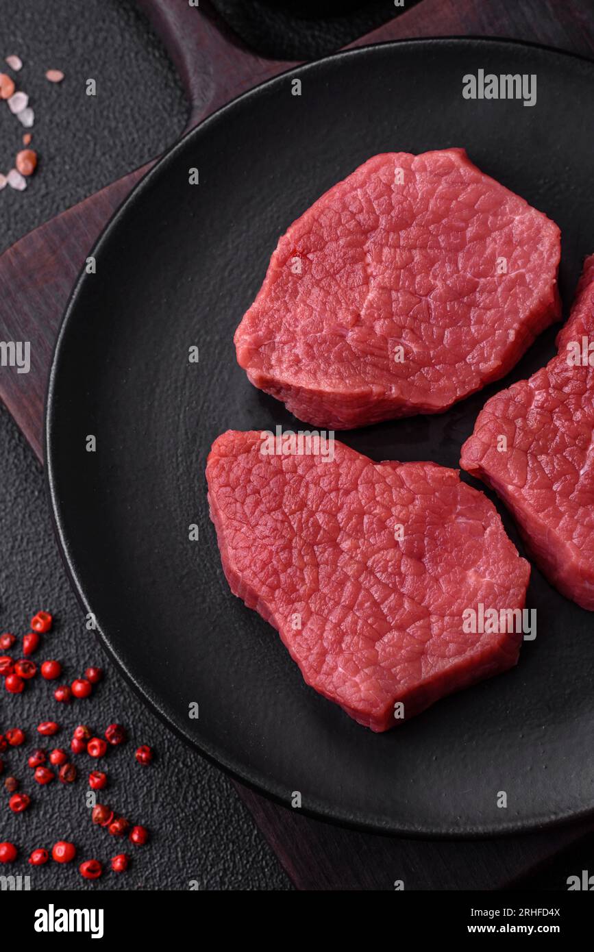Juicy fresh raw beef meat with salt, spices and herbs on a dark ...