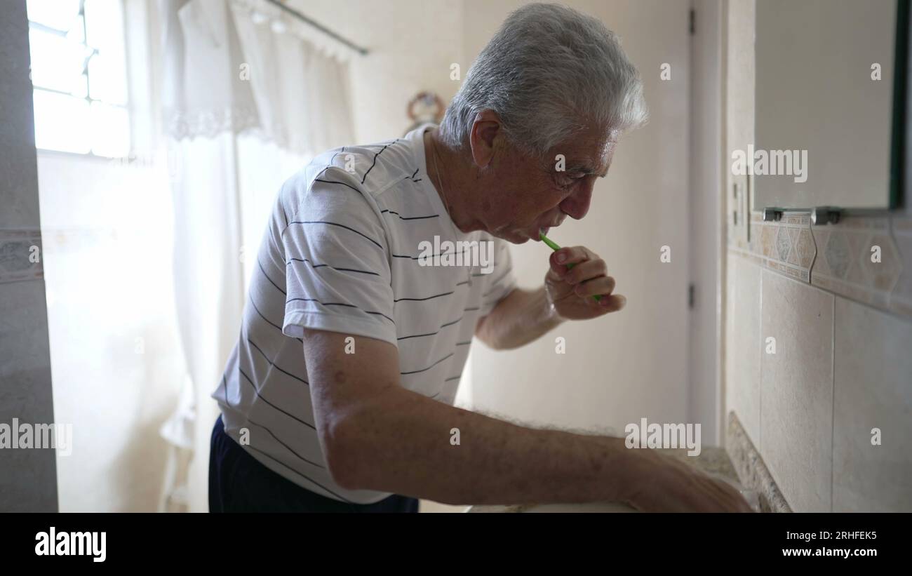 Senior man morning routine, washing face and brushing teeth in front of ...