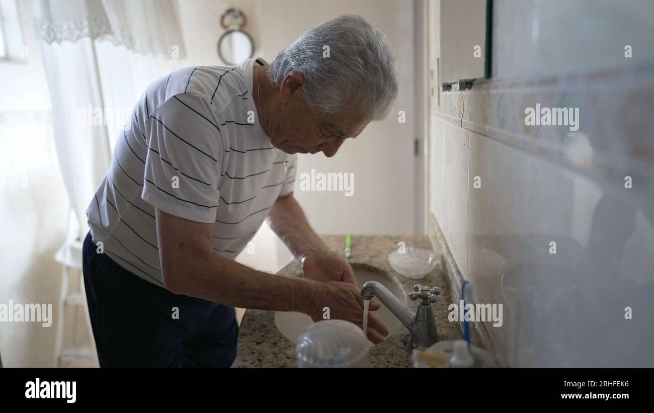 Senior man morning routine, washing face and brushing teeth in front of ...