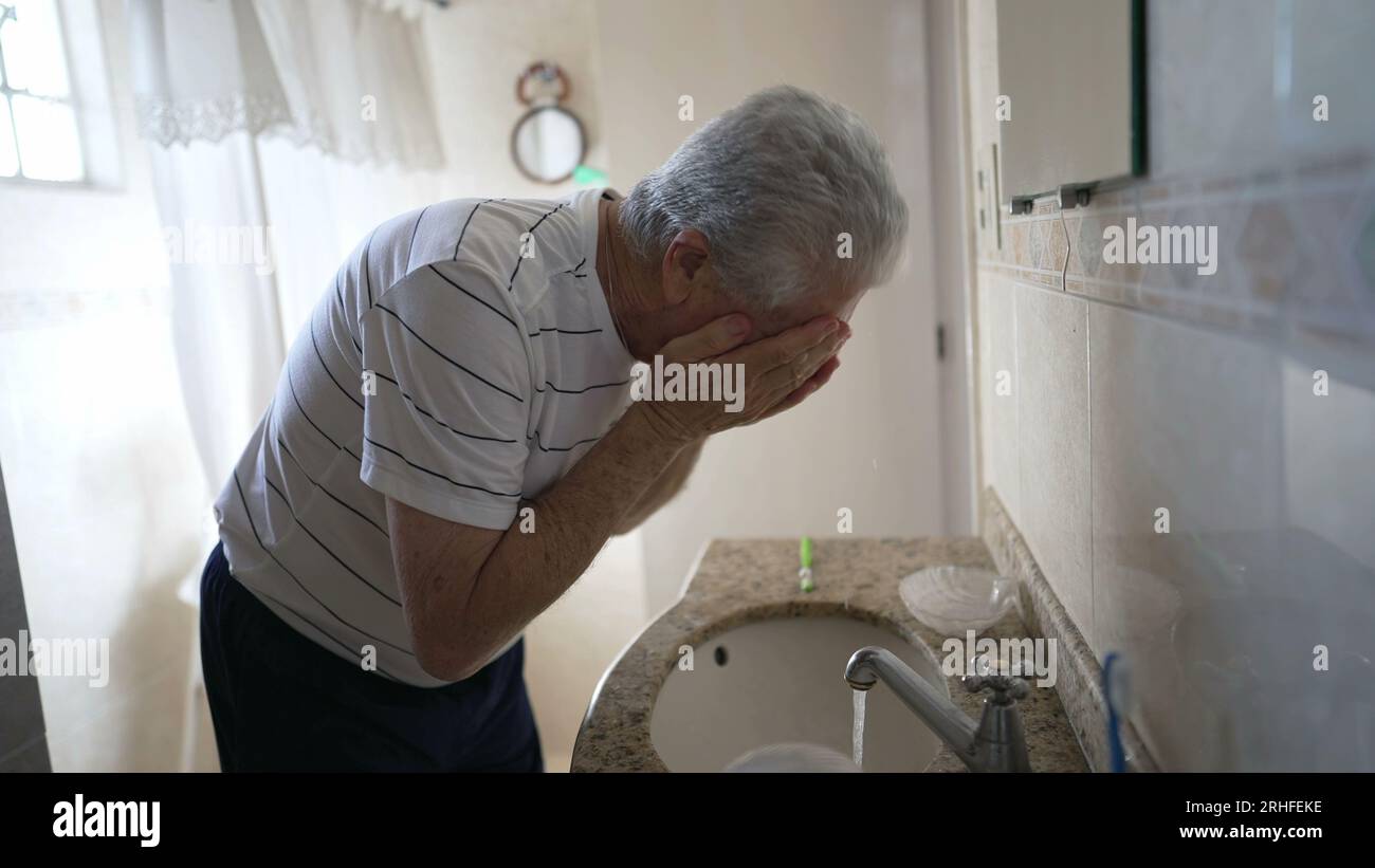 Senior man morning routine, washing face and brushing teeth in front of ...