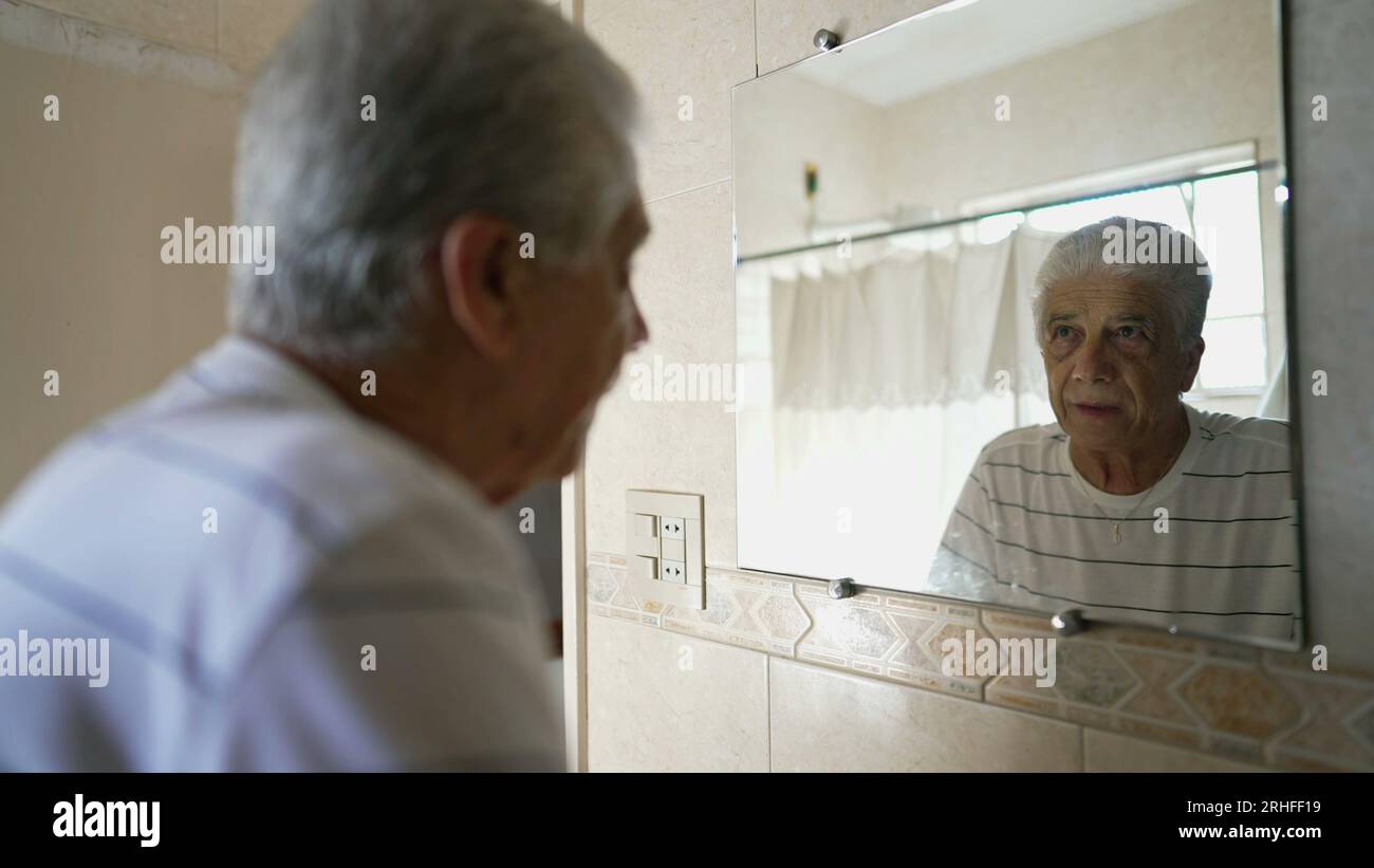 Older male caucasian man staring at his own reflection in bathroom ...