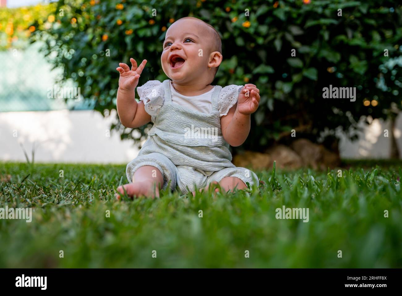 little baby sitting on the grass in the garden at home laughs out loud ...