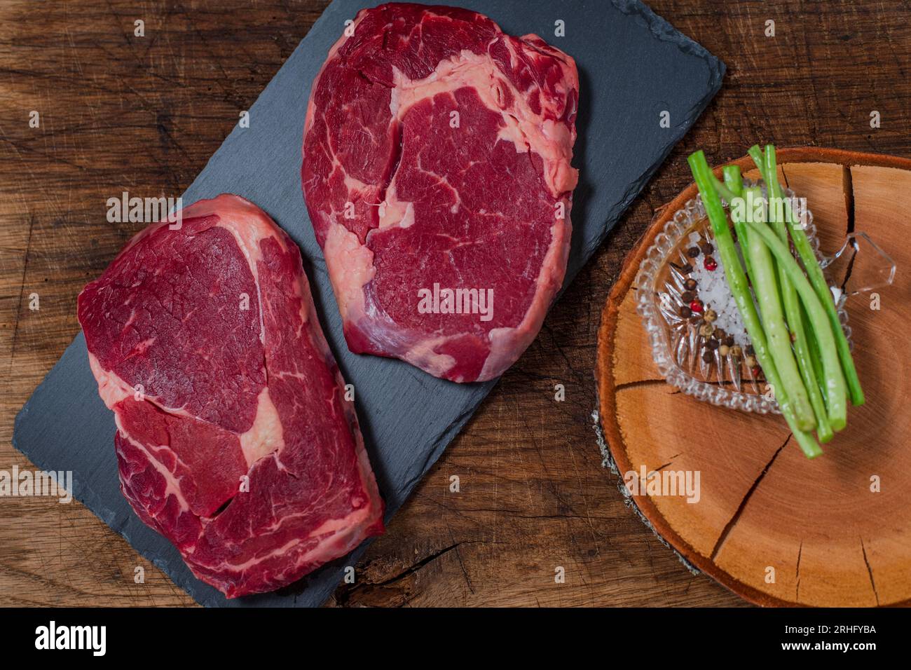 Two ribeye steaks with salt and pepper on the black cutting board ...