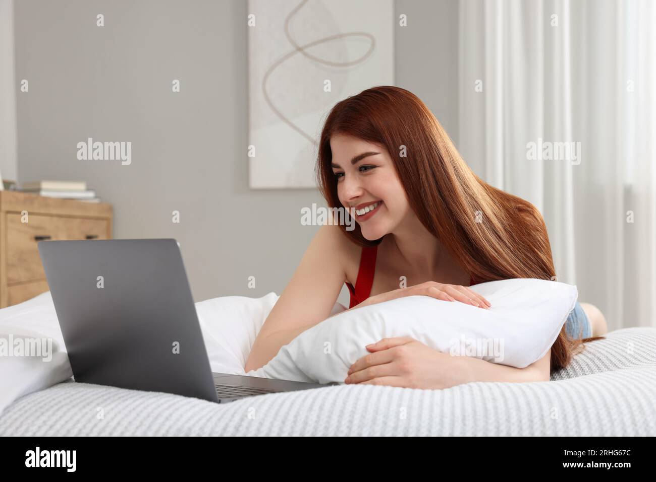 Happy woman with laptop on bed in bedroom Stock Photo - Alamy