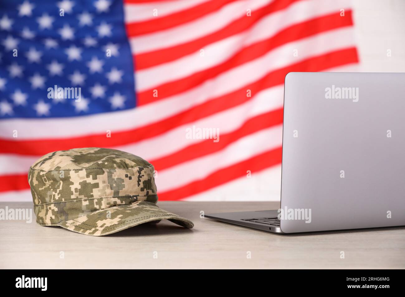 Cap and laptop on wooden table against flag of USA. Military education ...