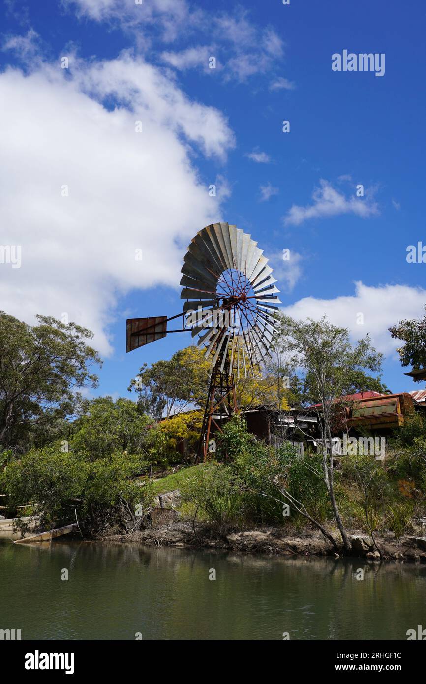 Historical vintage wind mill or water pump next to water with blue sky ...