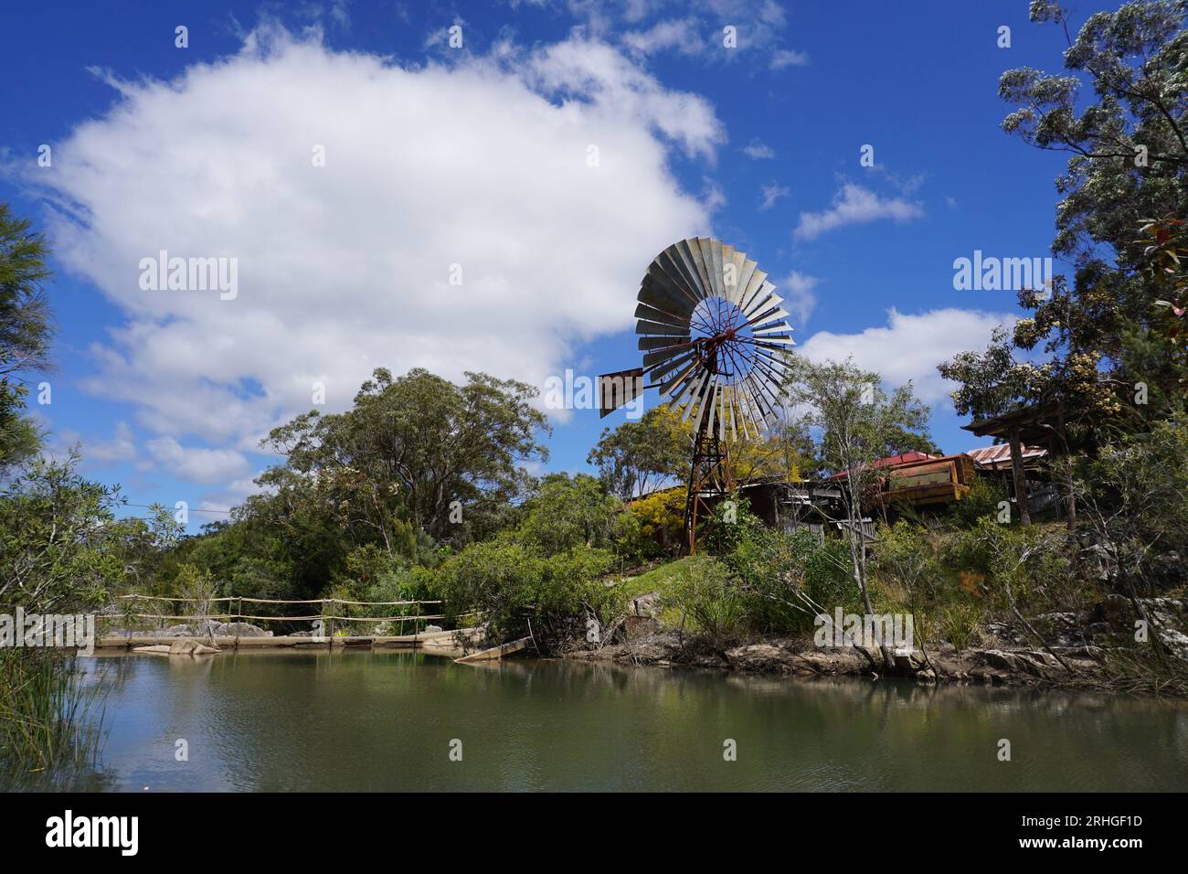 Historical vintage wind mill or water pump next to water with blue sky ...