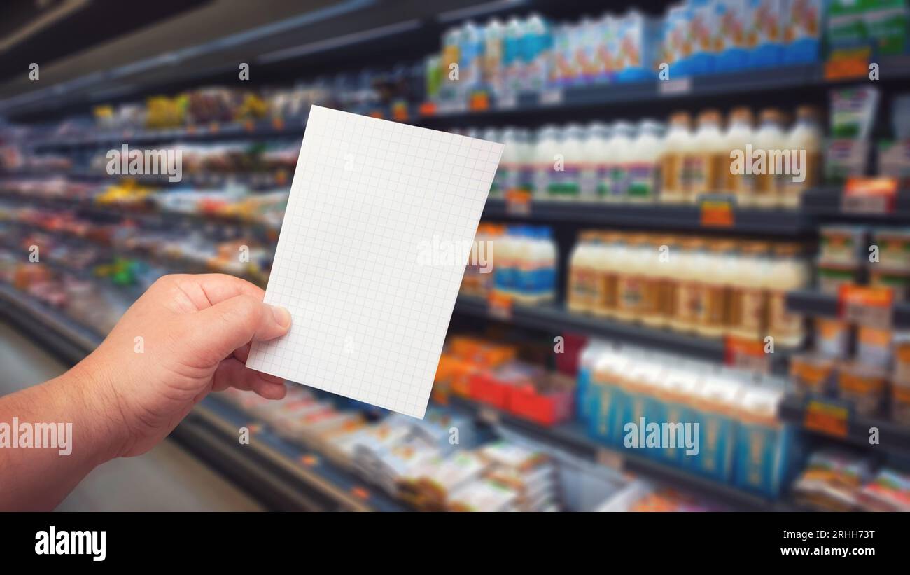 Hand with note paper at supermarket showcase background. Shopping list ...