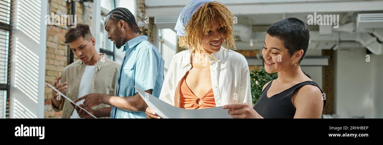 multicultural colleagues smiling, looking at project on papers ...