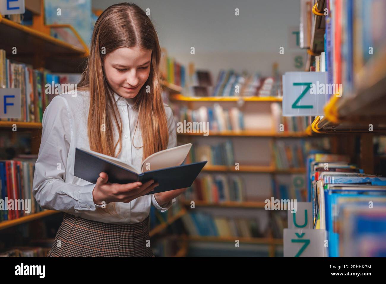 Schoolgirl searching and choosing books from a bookshelf in the library ...