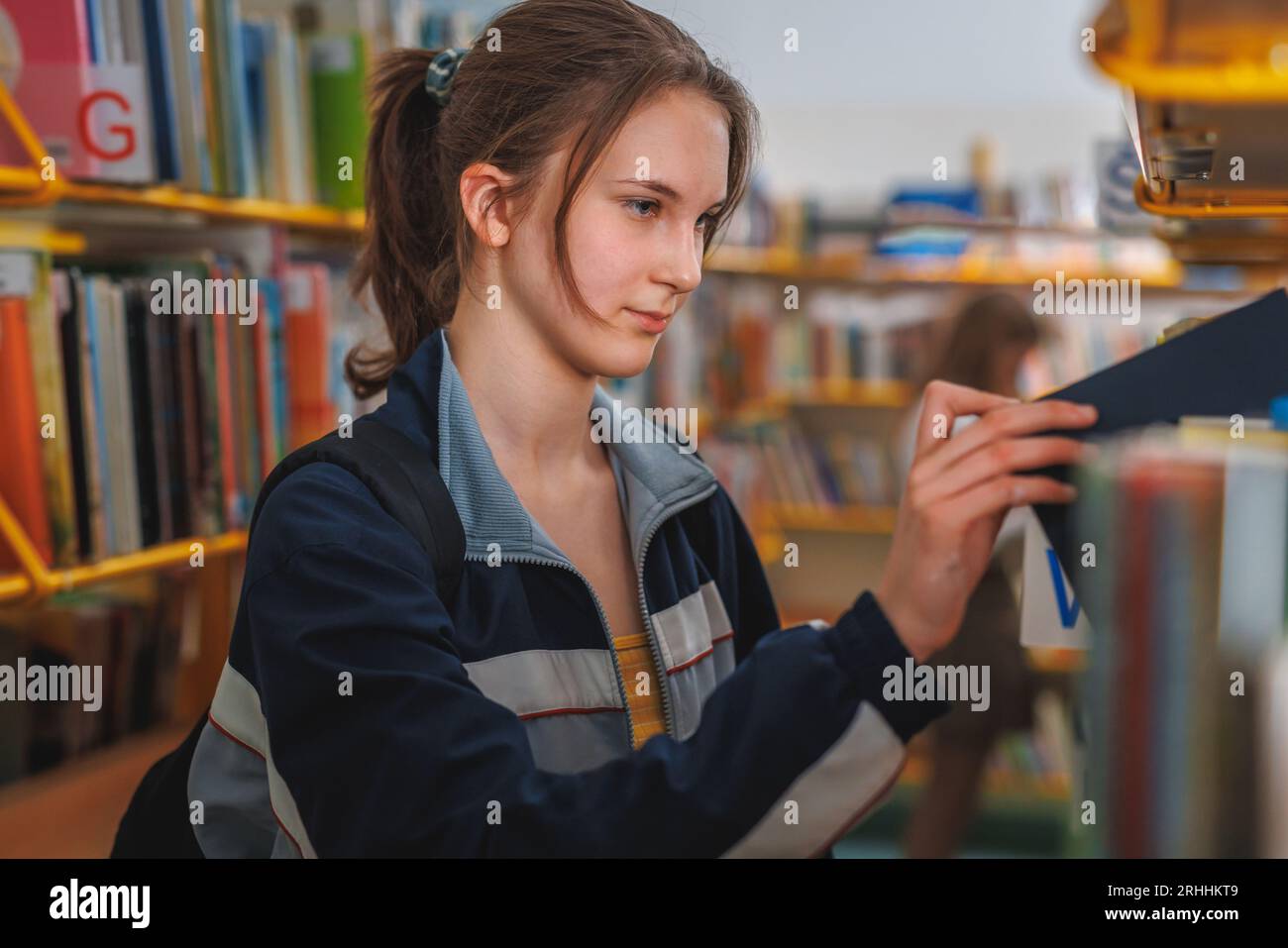 Schoolgirl searching and choosing books from a bookshelf in the library ...