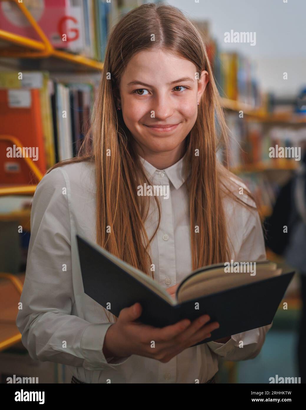 Schoolgirl searching and choosing books from a bookshelf in the library ...