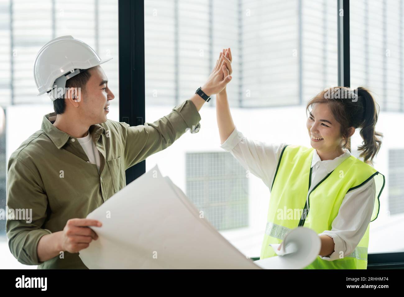 Construction engineer with blueprint making high five while standing on ...