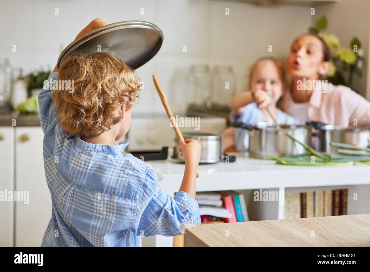 Boy playing with lid and ladle while looking at family in kitchen at ...