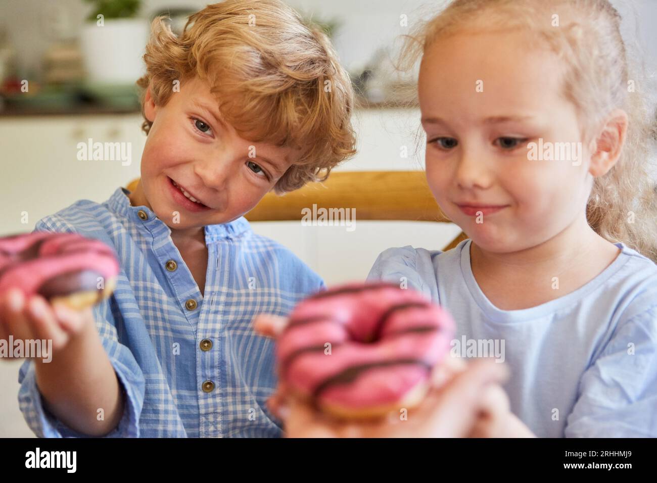 Curious siblings examining fresh donuts in kitchen at home Stock Photo ...