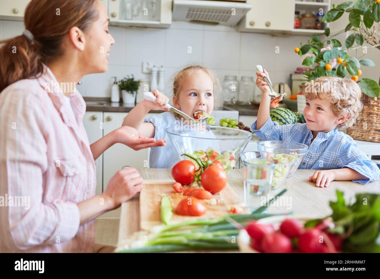 Son and daughter having fun while eating vegetable salad with mother in ...