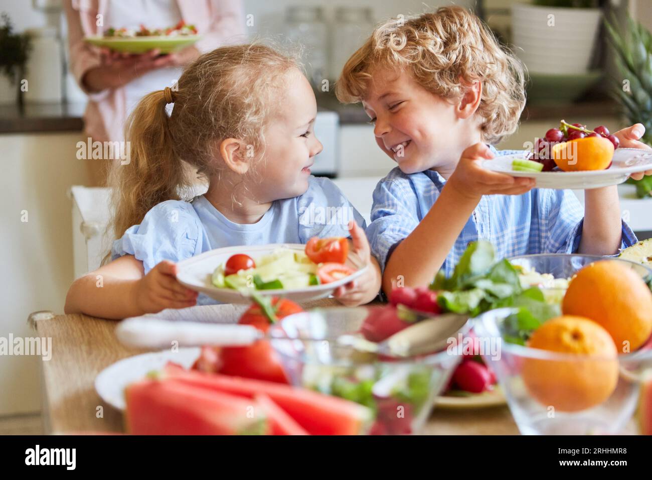 Two happy siblings eating fresh vegetables and fruits together in a ...
