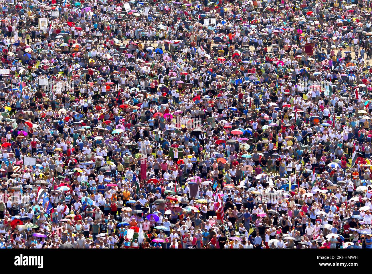 A dense, colorful crowd with umbrellas stands with unrecognisable faces ...
