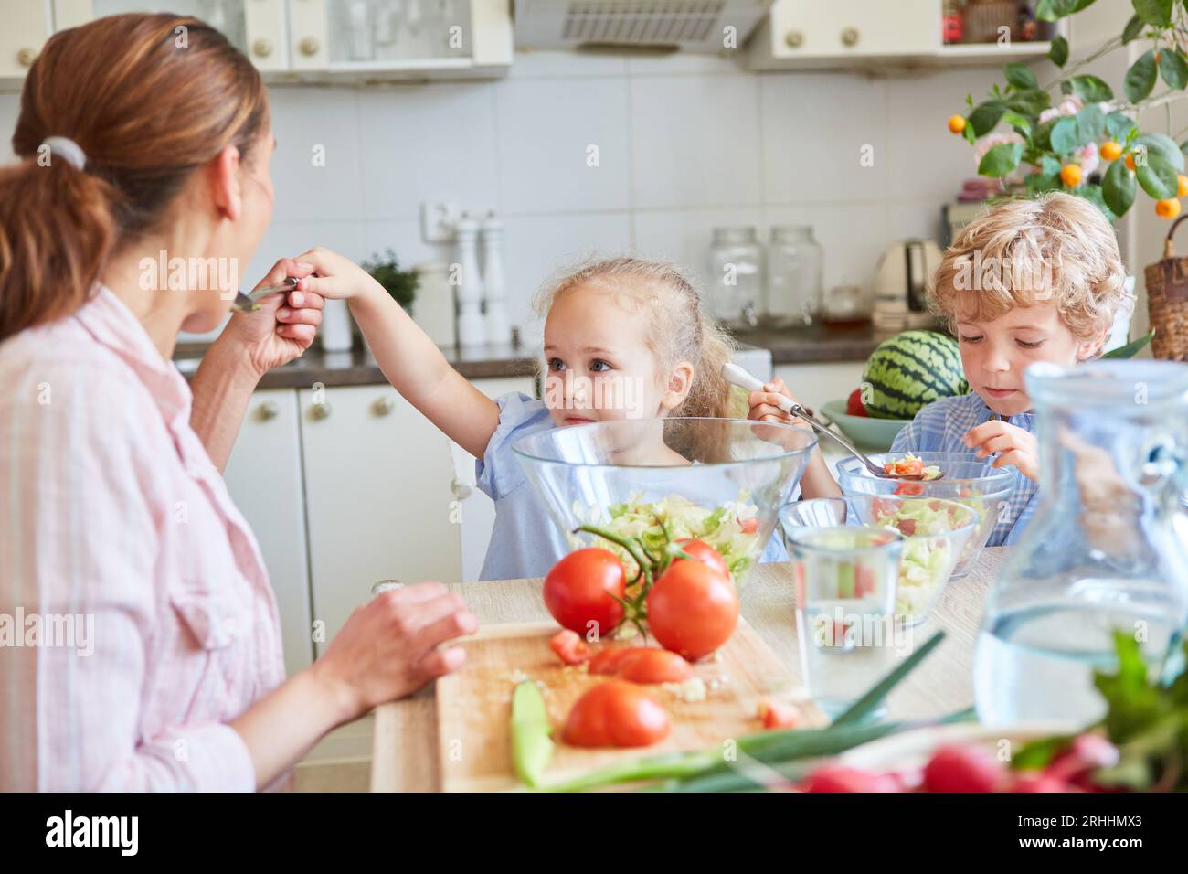 Mother tasting vegetable salad made by son and daughter in kitchen at ...