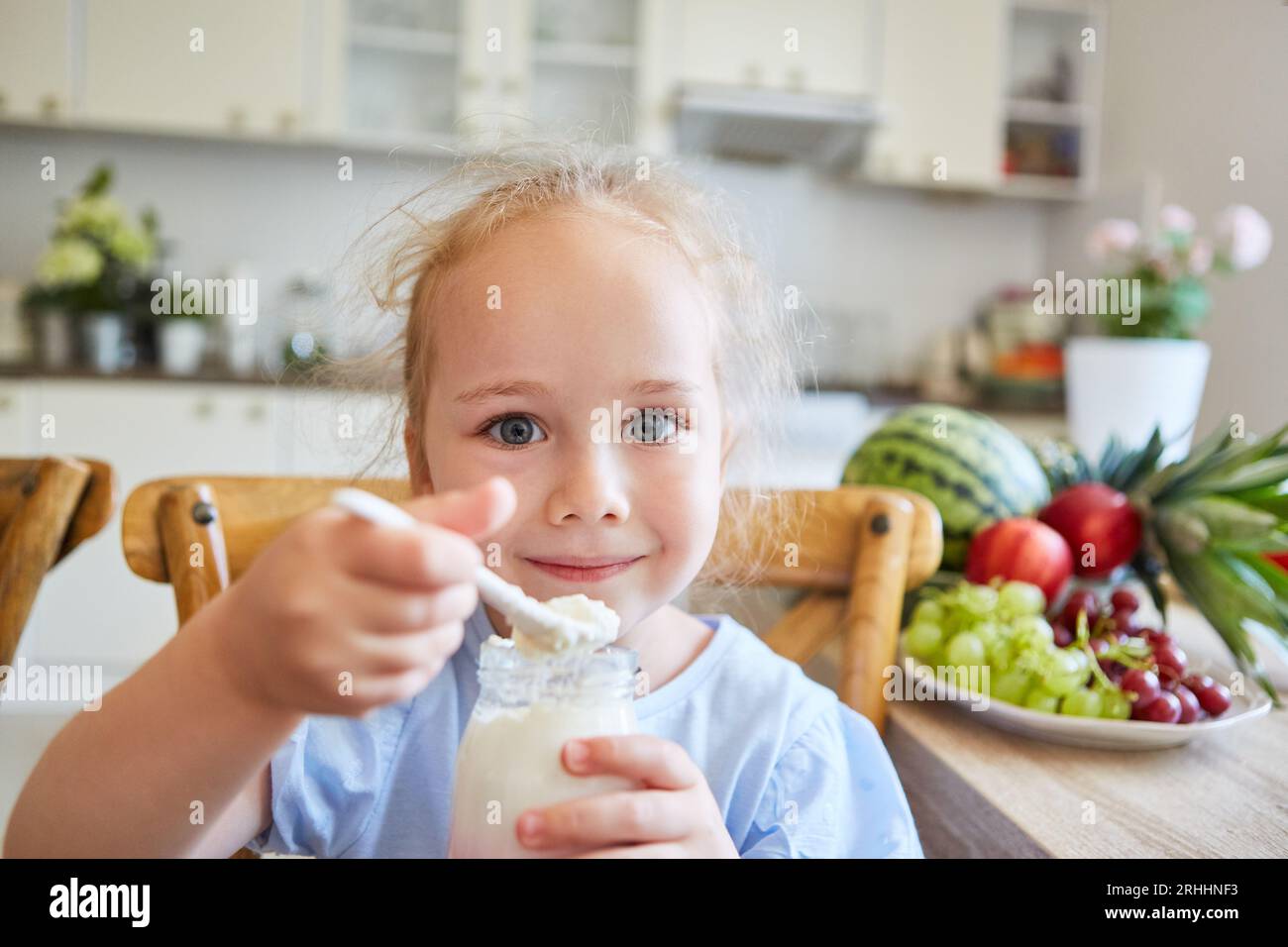 Portrait of smiling cute girl eating fresh yogurt parfait with spoon in ...