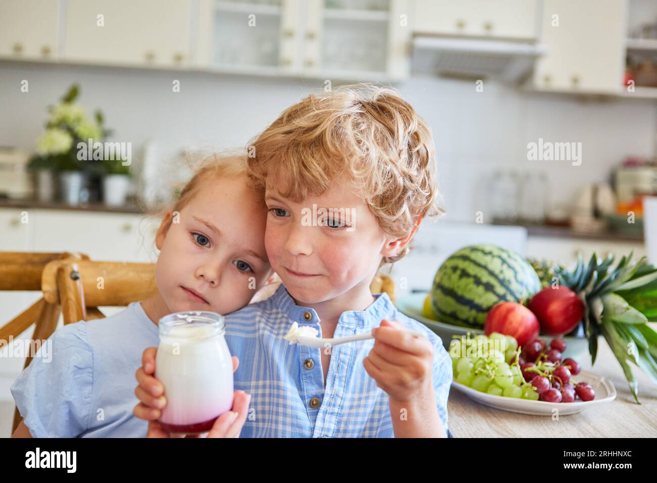 Blond boy eating parfait with sister leaning on shoulder while sitting ...