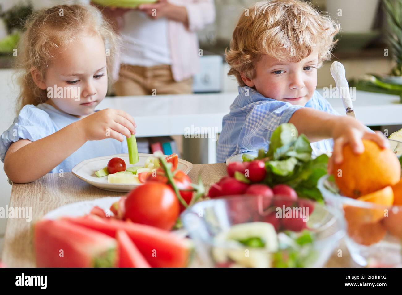 Boy reaching for oranges while making salad with sister in kitchen at ...